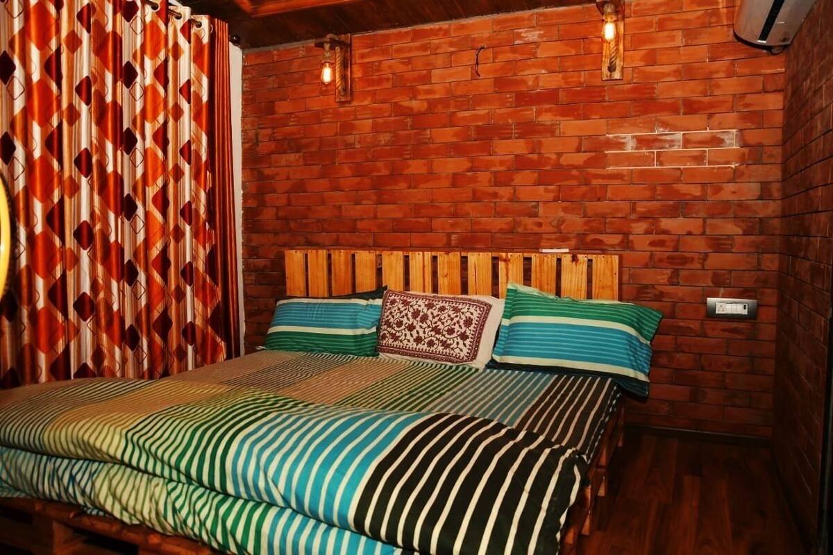 Quarto com parede de tijolos, cabeceira de madeira e cama com roupa de cama listrada.