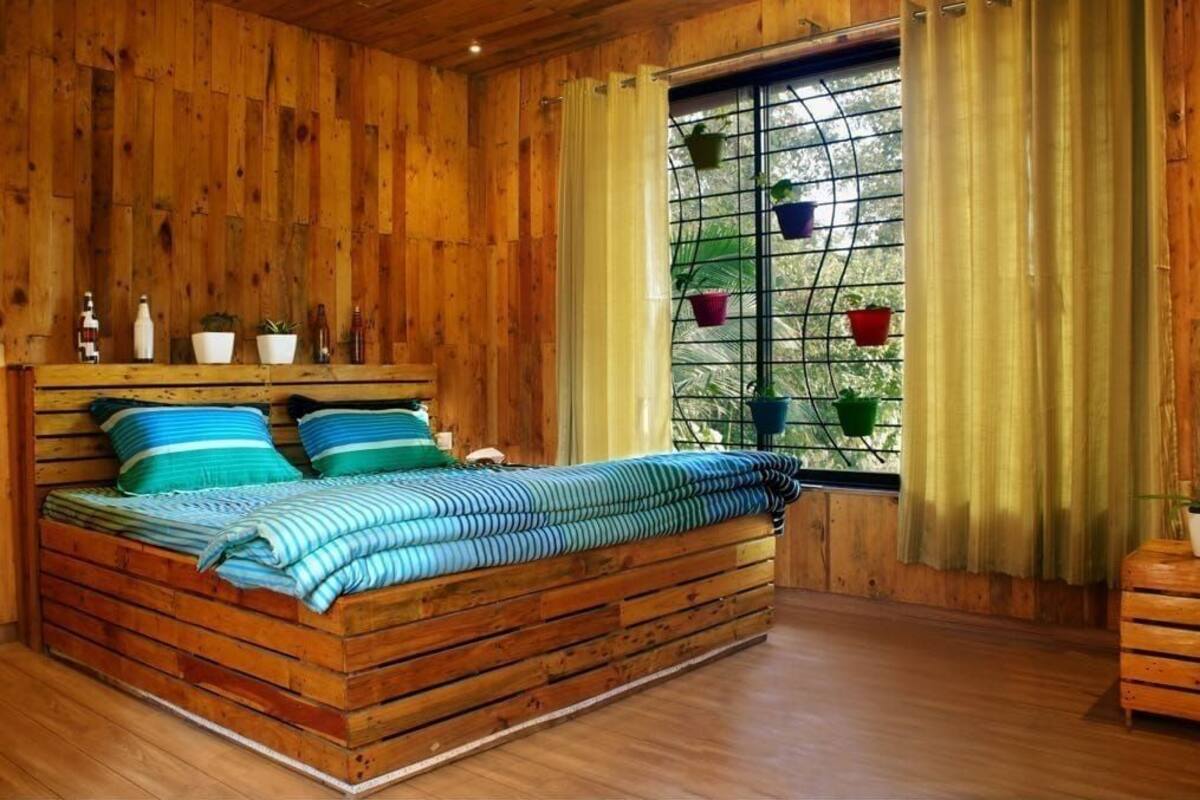 Quarto de cabana de madeira com cama, paredes de madeira, janela com plantas em vasos e cortinas.