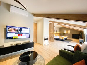 Quarto de hotel moderno com televisão de tela plana, sofá, cama e teto de madeira.