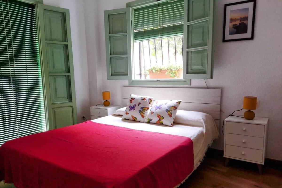 Quarto com cama, duas mesas de cabeceira, janela com persianas e um quadro na parede.