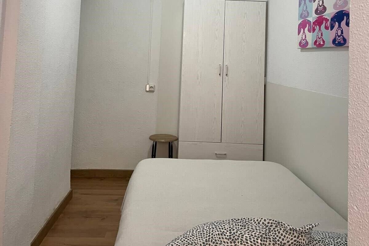 Quarto com cama, ventilador de teto, ar condicionado, guarda-roupa e parede com pôster colorido.