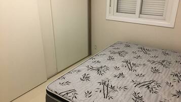 Um quarto com uma cama coberta por um edredom estampado com motivos de bambu, um guarda-roupa fechado e uma janela com persianas.