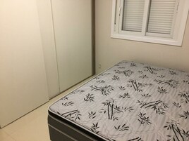 Um quarto com uma cama coberta por um edredom estampado com motivos de bambu, um guarda-roupa fechado e uma janela com persianas.