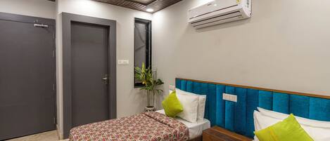Quarto de hotel com duas camas, cabeceira de madeira, planta em vaso e ar condicionado.