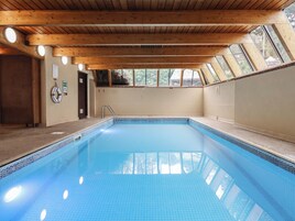 Piscina interna com vigas de madeira, boia salva-vidas e placa de segurança.