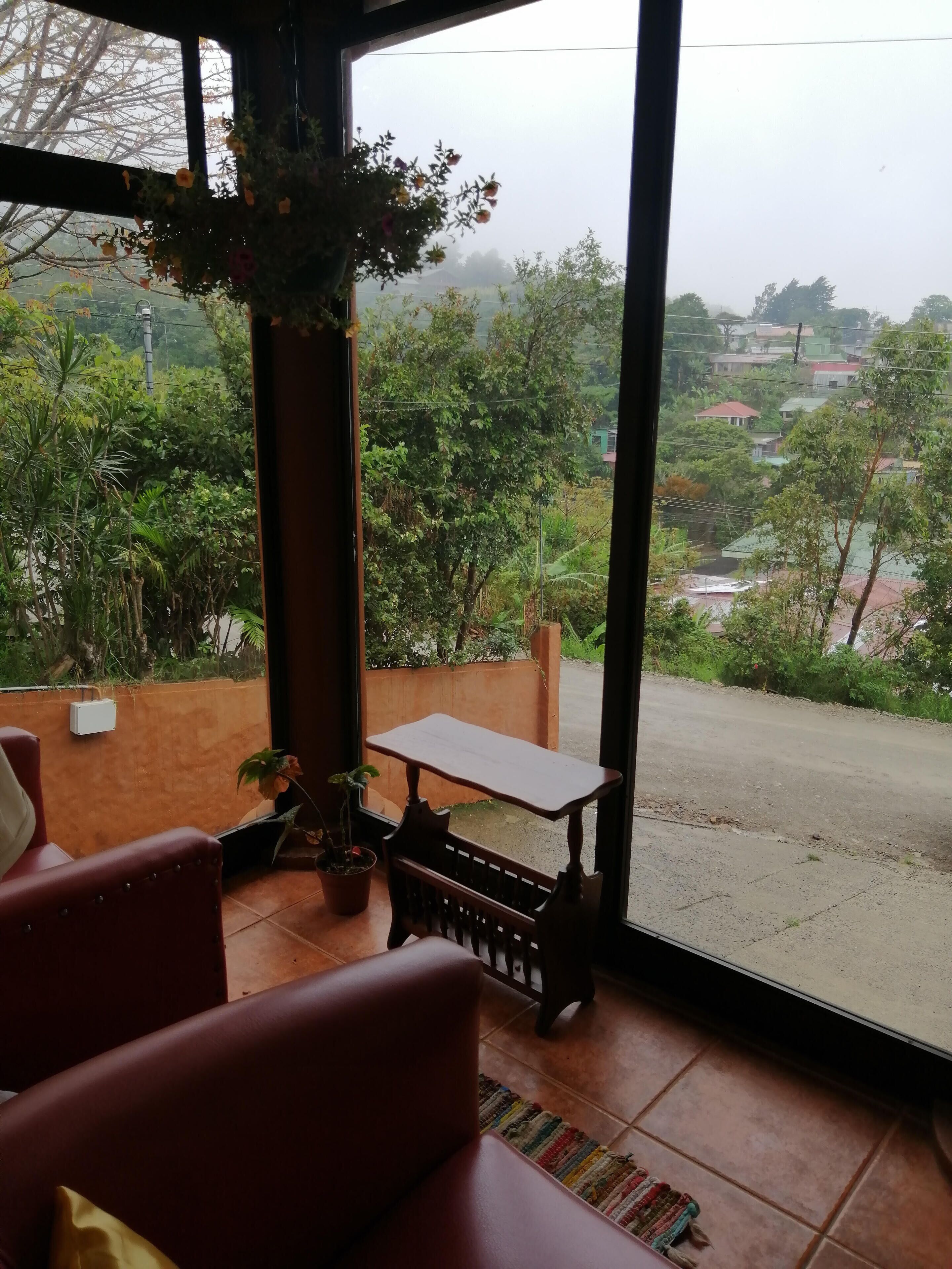 Quarto com uma grande janela, uma mesa de madeira, um sofá vermelho e um vaso com planta.