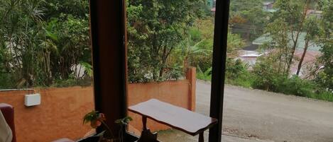 Quarto com uma grande janela, uma mesa de madeira, um sofá vermelho e um vaso com planta.