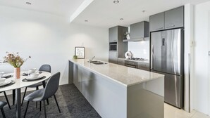 Uma cozinha moderna com uma ilha central, eletrodomésticos de aço inoxidável e uma área de refeições com mesa e cadeiras.