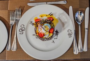 Sobremesa em um prato branco com grade de chocolate, morangos e um molho amarelo.