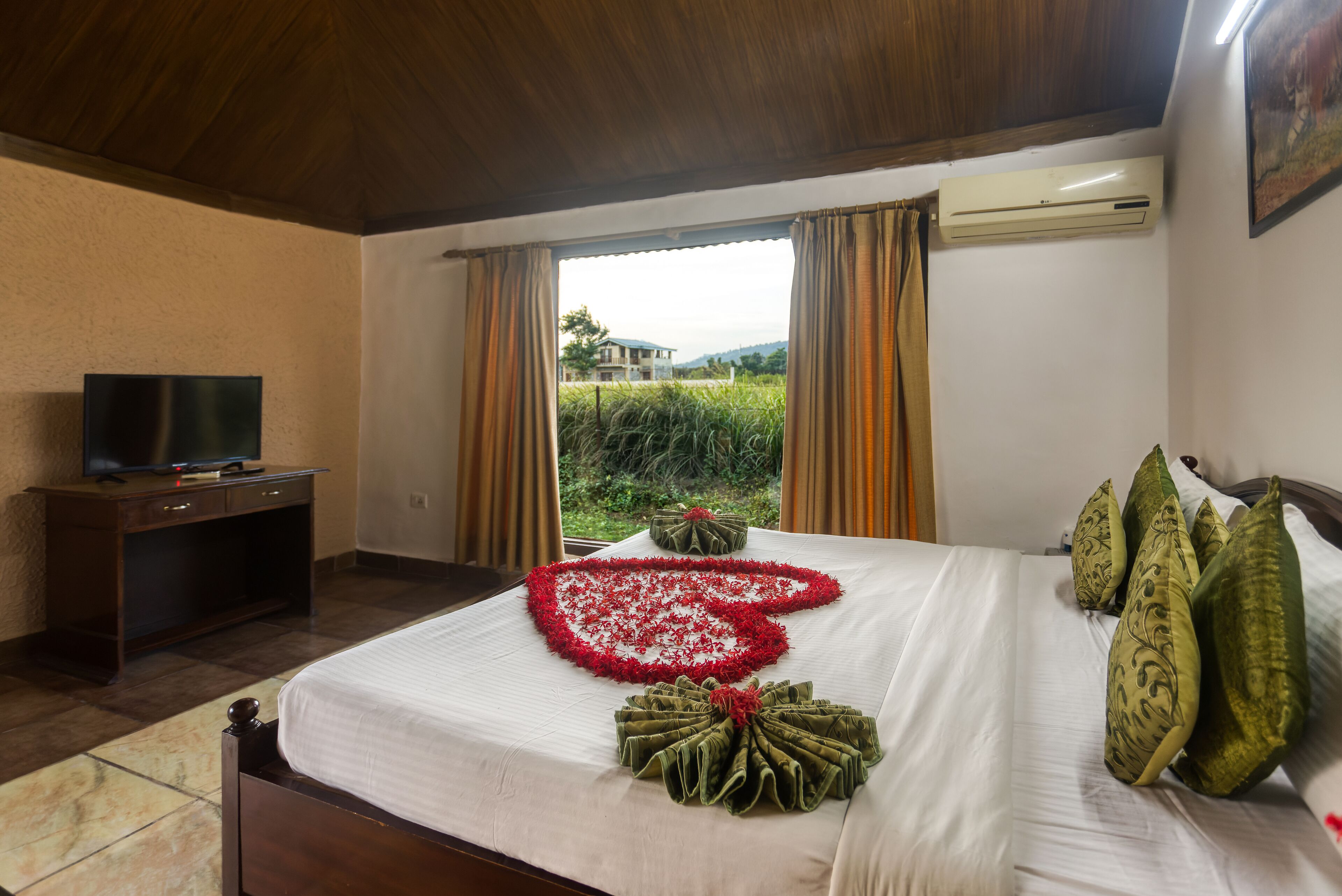 Quarto de hotel com uma cama, uma televisão sobre um armário de madeira e vista para o verde lá fora.