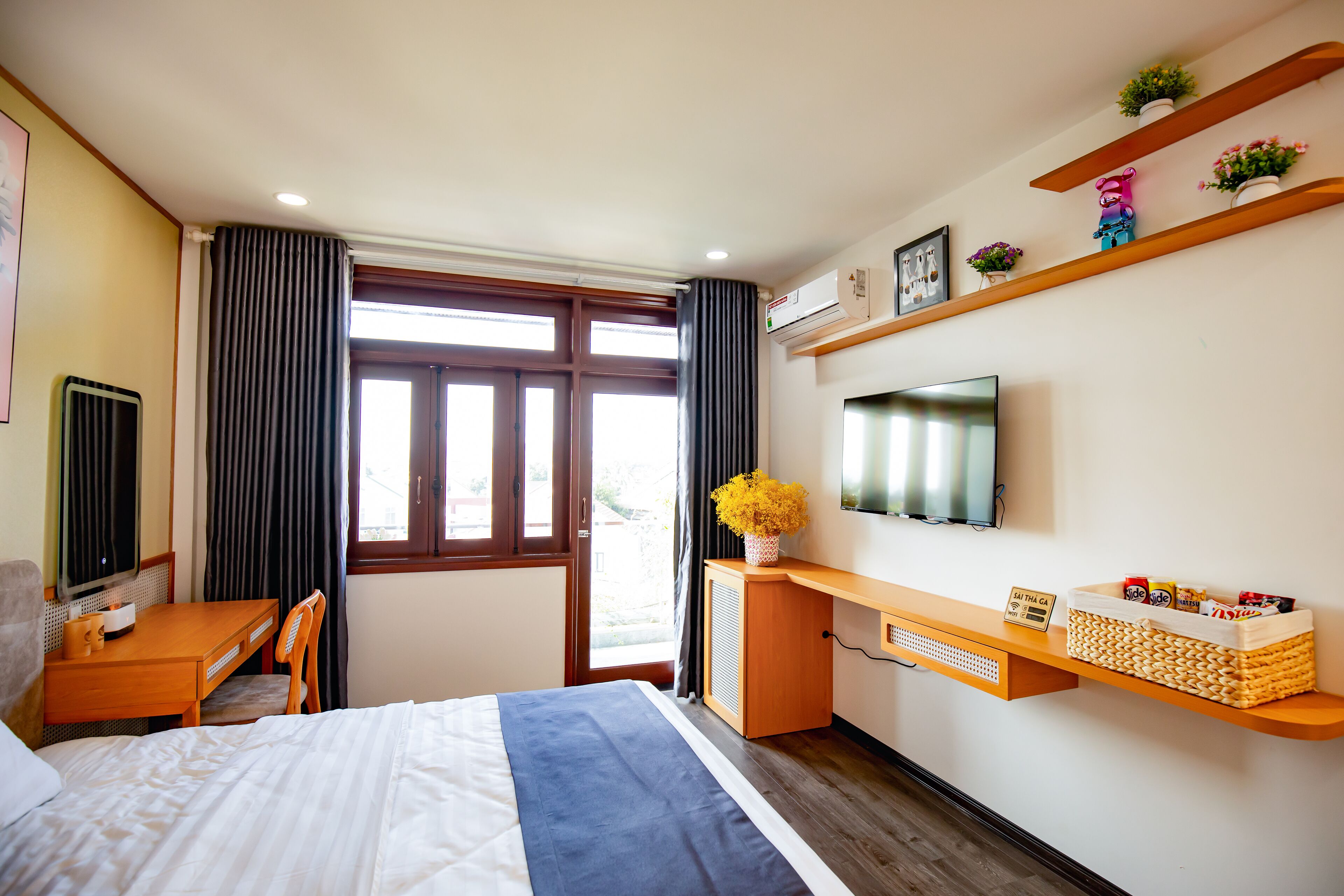 Quarto de hotel com cama, escrivaninha, cadeira, televisão e janela com cortinas.
