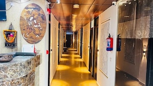Corredor de hotel com uma receção em mármore, uma obra de arte em madeira e extintores.