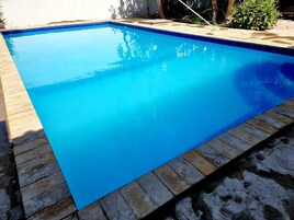 Piscina retangular com borda azulejada em azul, rodeada por um deck de pedra e uma borda de concreto.