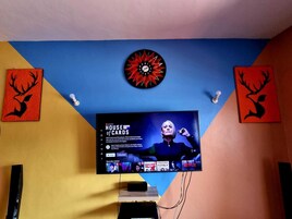 Uma televisão fixada na parede, com um relógio decorativo em cima.