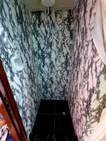 Um banheiro com piso de azulejos pretos, um vaso sanitário branco e parede com padrão marmorizado.