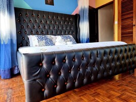 Quarto com cabeceira estofada, piso de madeira e roupa de cama estampada.