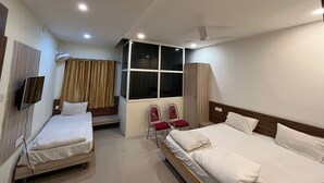 Quarto de hotel com duas camas de solteiro, televisão, ar condicionado, janela com cortinas e ventoinha no teto.