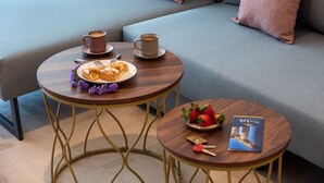 Um quarto acolhedor com um sofá, duas mesas redondas com chávenas de café, pastelaria e um livro.