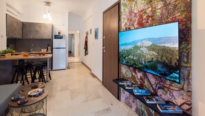 Uma cozinha moderna com uma grande televisão de tela plana na parede, uma área de jantar com mesa e cadeiras, e um corredor que leva a um quarto.