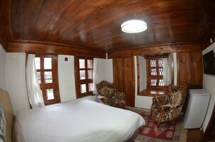 Quarto com painéis de madeira, uma cama, duas cadeiras, um frigorífico e um candelabro.