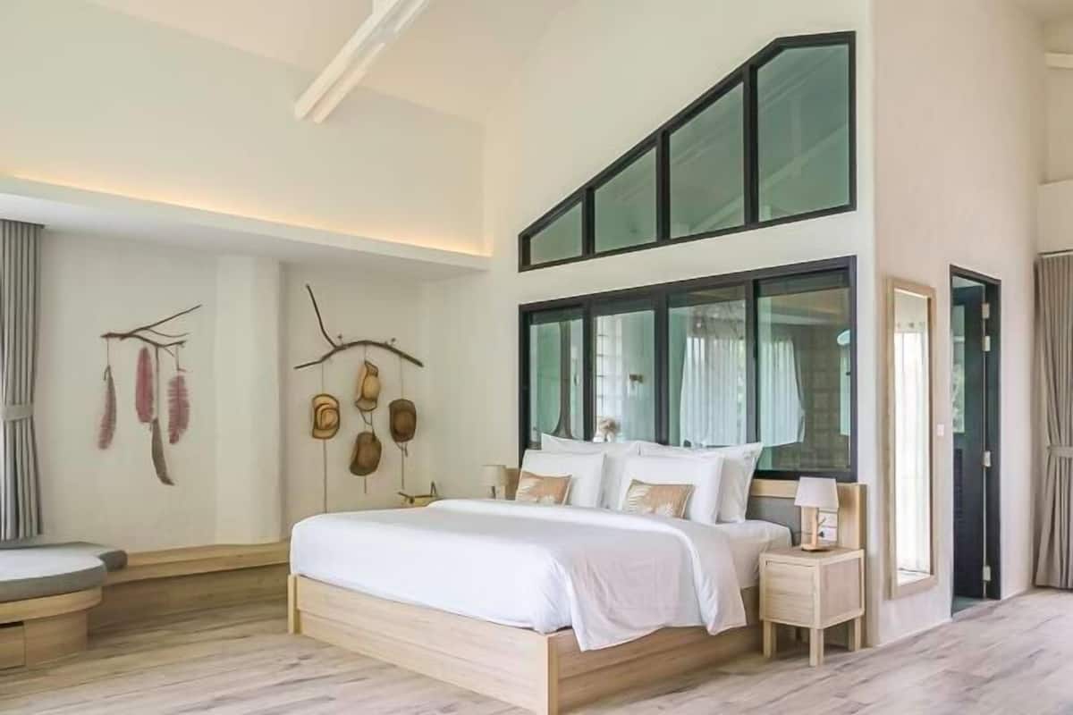Quarto moderno com uma cama grande, uma mesa de cabeceira pequena e uma janela ampla.