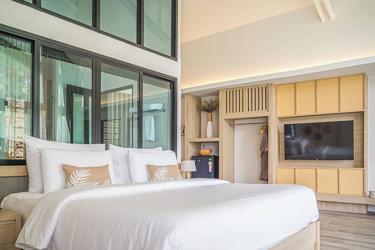 Quarto de hotel moderno com uma cama grande, uma TV de tela plana na parede e um armário embutido de madeira.