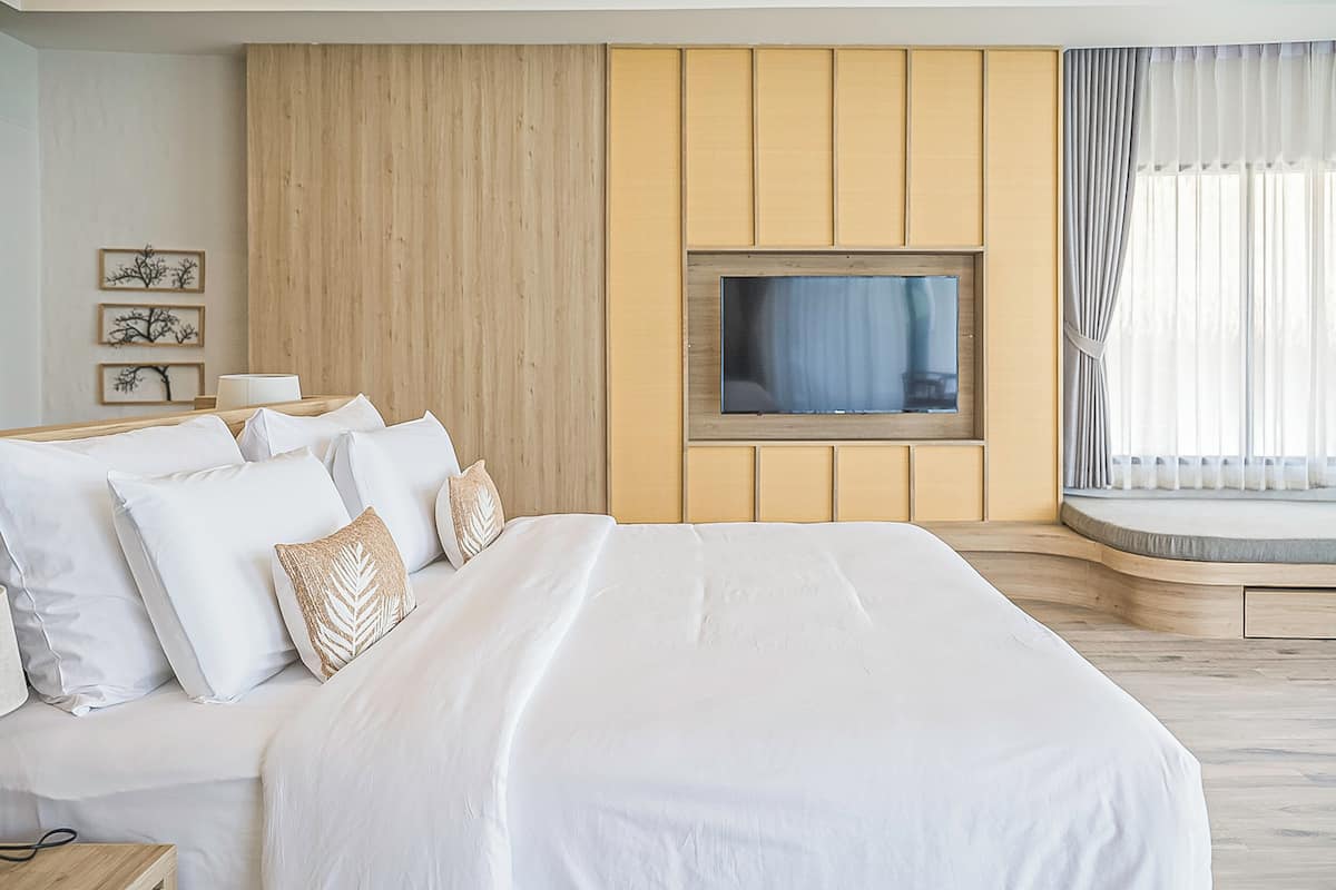 Quarto de hotel moderno com uma cama grande, televisão de tela plana na parede e janela com cortinas.