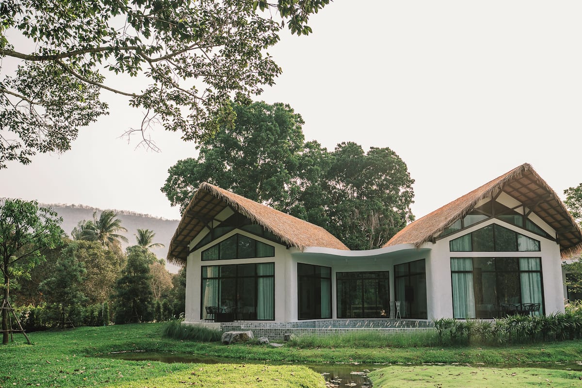Uma casa moderna com telhado de palha, janelas grandes e um jardim com lago.