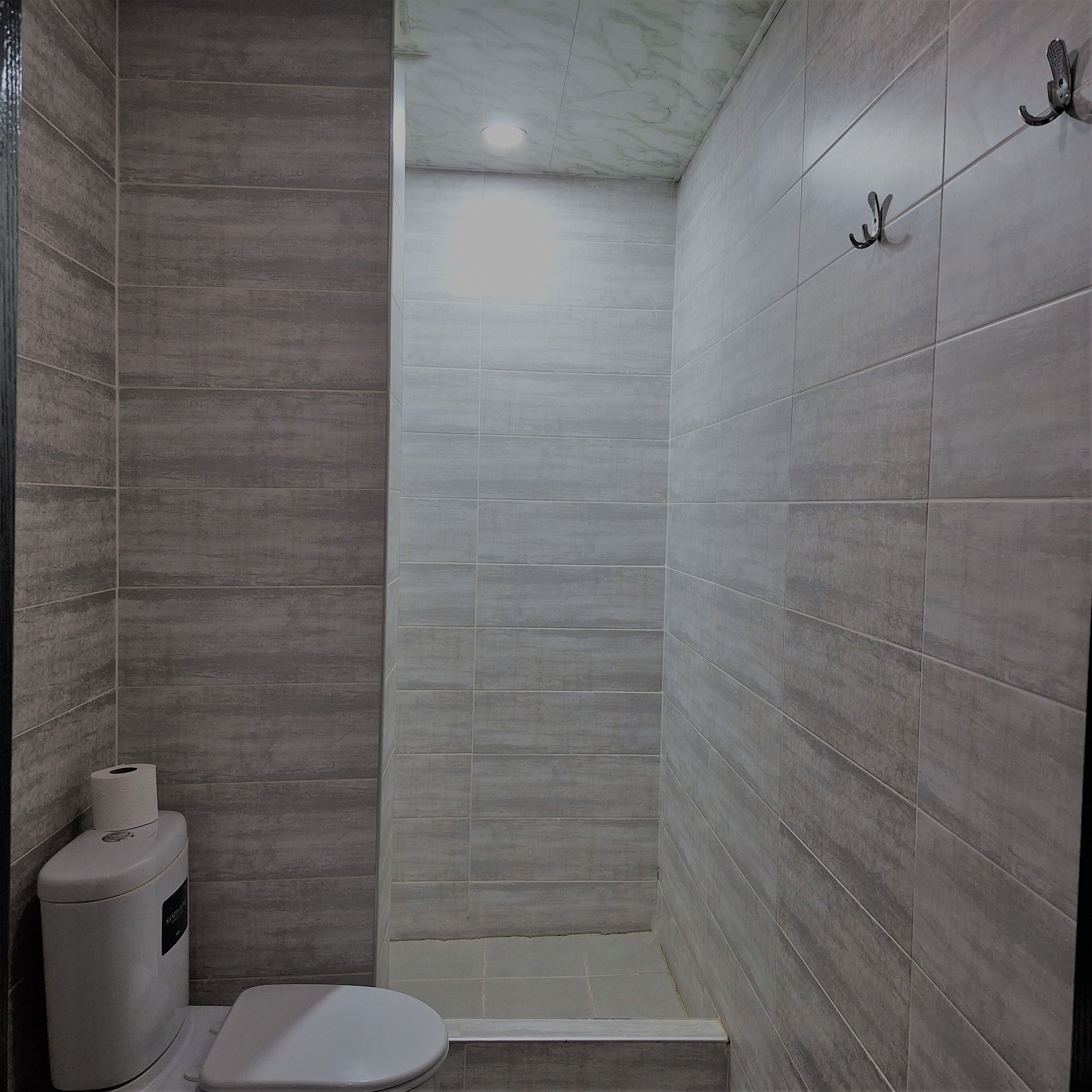 Uma casa de banho pequena e moderna, com azulejos cinzentos, sanita e zona de duche.