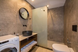 Um banheiro moderno com máquina de lavar, pia com cuba grande, vaso sanitário e chuveiro com divisória de vidro.