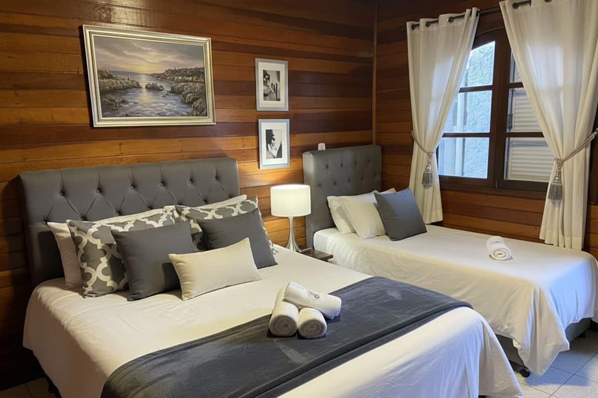 Quarto de hotel com duas camas, parede de madeira, um quadro e uma janela com cortinas.