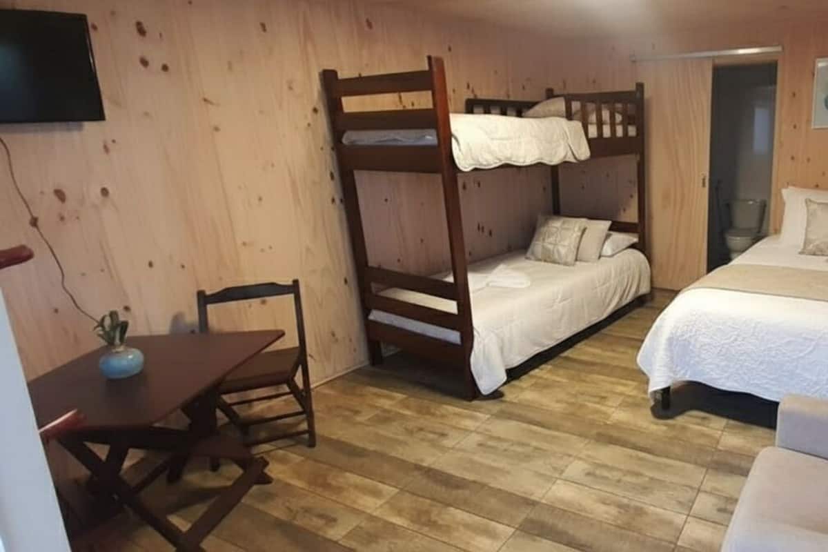 Quarto estilo cabana de madeira com beliches, sofá e mesa de jantar.