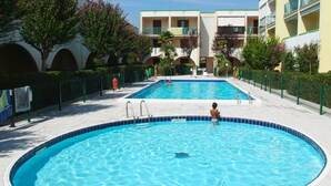 Uma grande piscina ao ar livre com um deck revestido de azulejos, cercada por uma vedação e árvores.