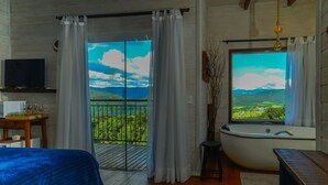 Quarto com cama grande, banheira, televisão e varanda com vista panorâmica.