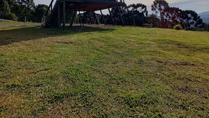Um edifício moderno com telhado triangular e grandes janelas, localizado em um campo gramado com árvores ao fundo.