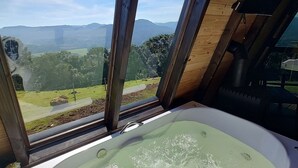 Uma banheira de hidromassagem com vista para uma paisagem montanhosa através de grandes janelas.