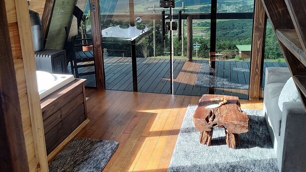 Um amplo quarto no estilo loft com um grande claraboia, piso de madeira, um espaço de estar aconchegante e vista para o campo.