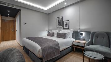 Um quarto moderno com cama, mesa de cabeceira, luminária, poltrona e uma pequena mesa redonda.