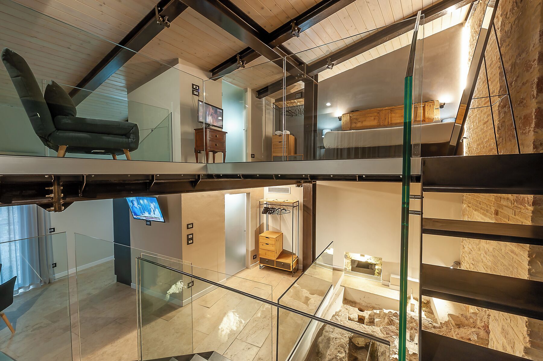Interior moderno com escada de vidro que liga dois andares, área de estar com sofá e televisão à vista.