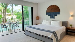Quarto moderno com cama grande, ventoinha no teto, vista para piscina e área de refeições com cadeiras.
