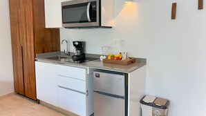 Cozinha compacta com micro-ondas, cafeteira e uma fruteira no balcão.