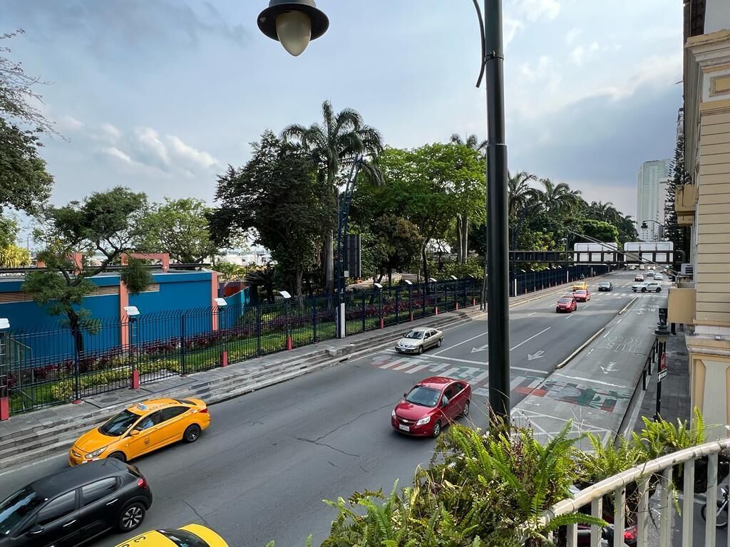 Vista da rua com carros, um edifício azul e uma cerca.
