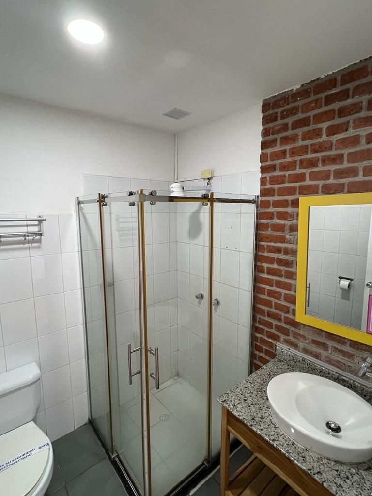 Casa de banho com chuveiro em cabine de vidro, sanita branca, lavatório com bancada de granito e espelho com moldura amarela.