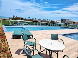 Uma área de piscina no terraço com vista clara para o oceano, piscina e espreguiçadeiras.
