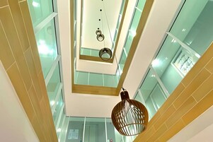 Interior moderno com teto alto, guarda-corpos de vidro e luminária pendente.