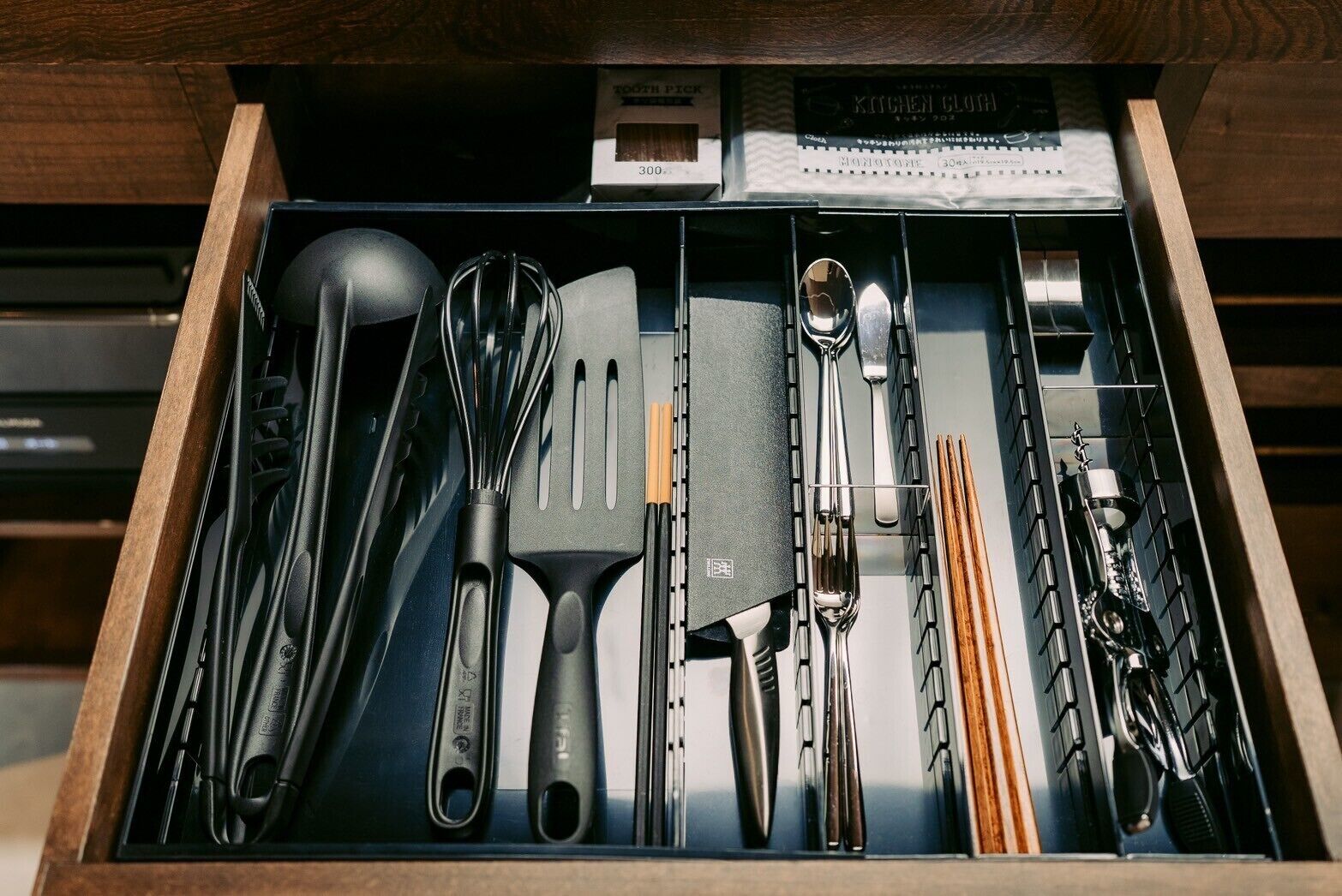 Uma gaveta com diversos utensílios de cozinha, incluindo batedores, espátulas, pinças e um ralador.