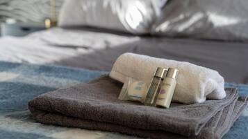 Toalha dobrada e duas embalagens de loção sobre a cama, com colcha estampada em azul e branco.