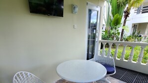 Uma área de estar ao ar livre coberta, com uma mesa branca e duas cadeiras de vime com almofadas azuis.