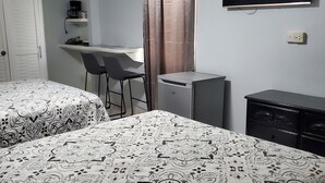 Quarto de hotel com duas camas, uma escrivaninha com cadeira, televisão e ventoinha no teto.