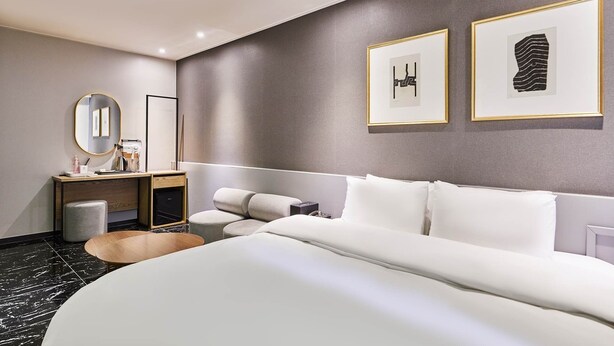 Quarto de hotel moderno com uma cama grande, uma mesa de cabeceira com abajur, um espelho e duas obras de arte emolduradas na parede.